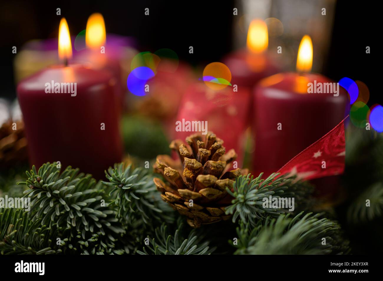 Shallow focus pine cone on advent wreath with four lit candles and ...