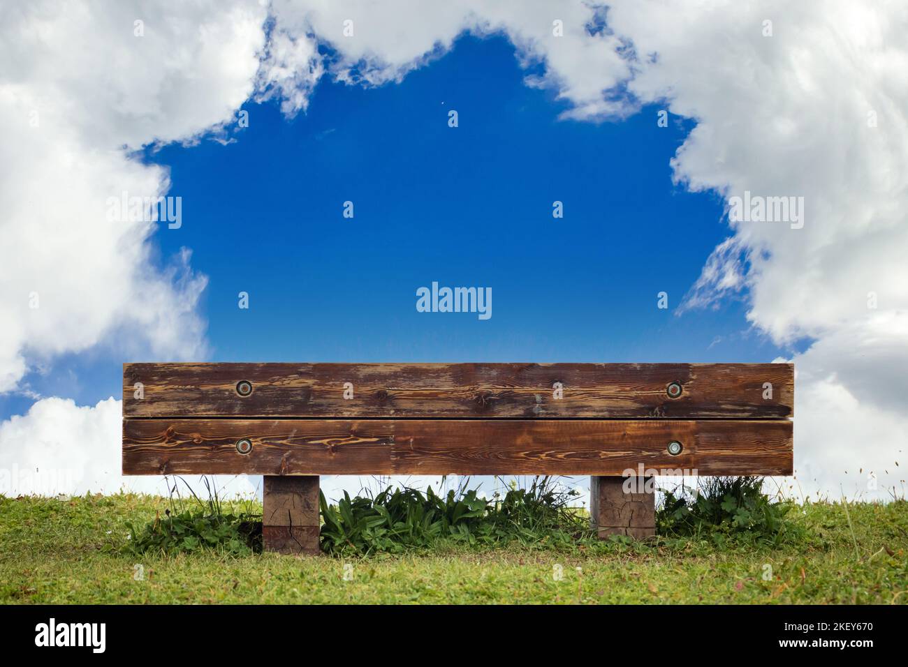 Wooden bench on a summer green lawn against a blue sky with clouds ...