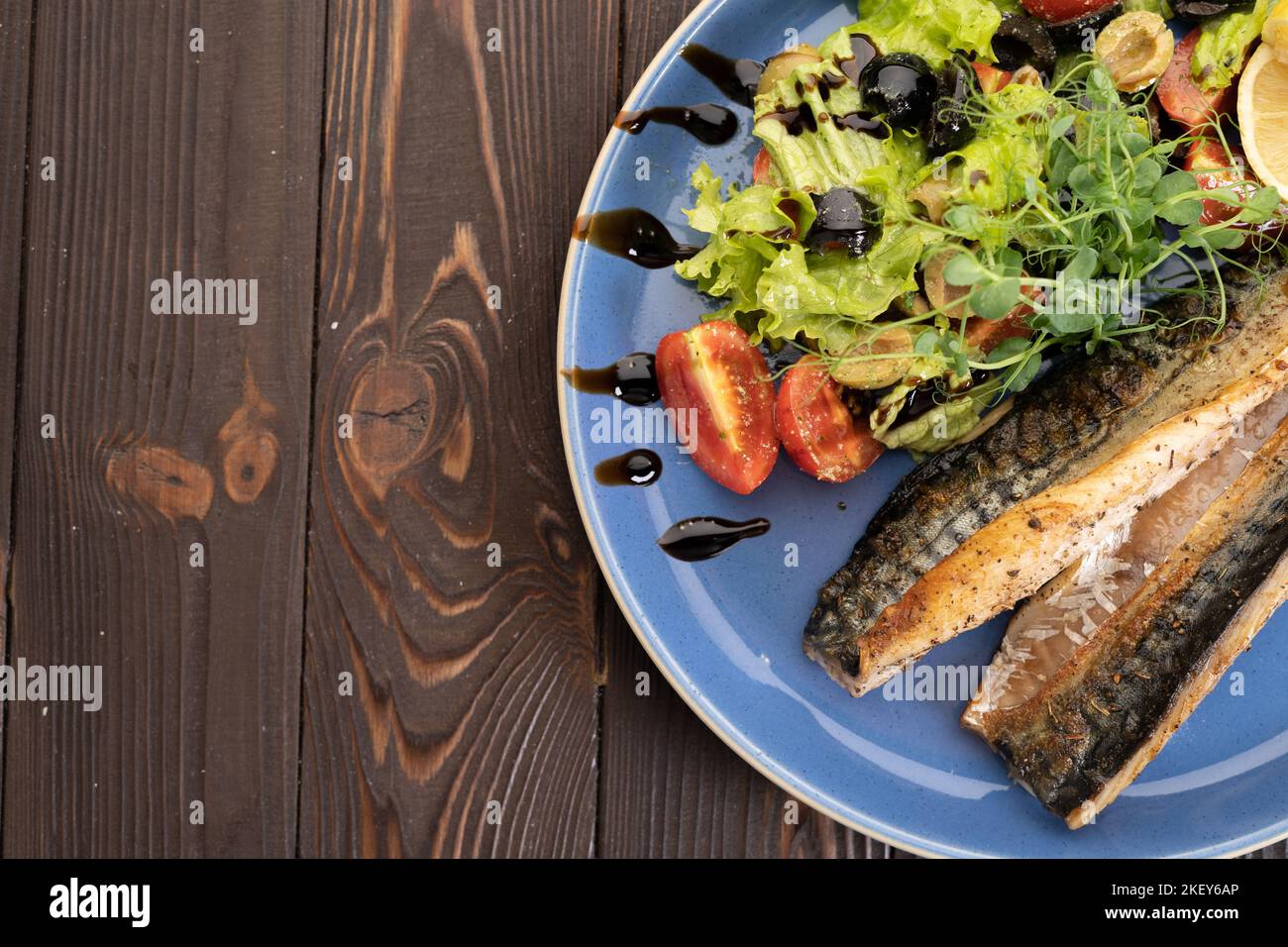Grilled fish fillet on plate with lemon and green salad on wooden ...