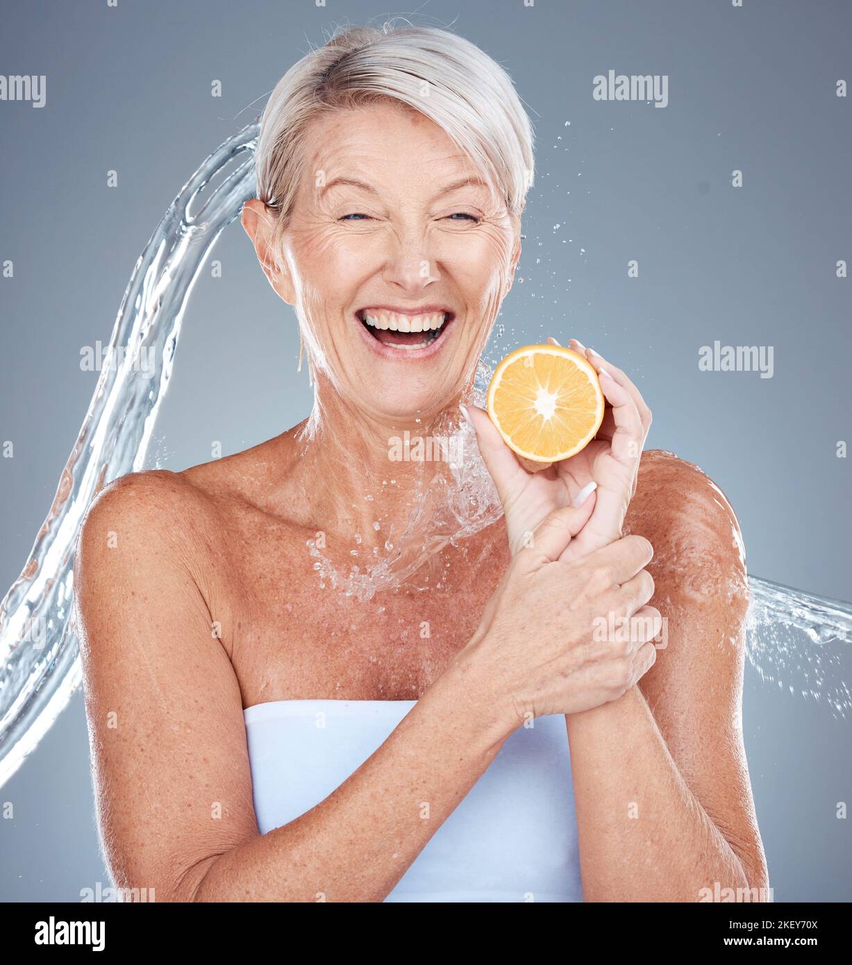 Woman, water splash and lemon for senior healthcare or skincare beauty. Elderly model, vitamin c ...