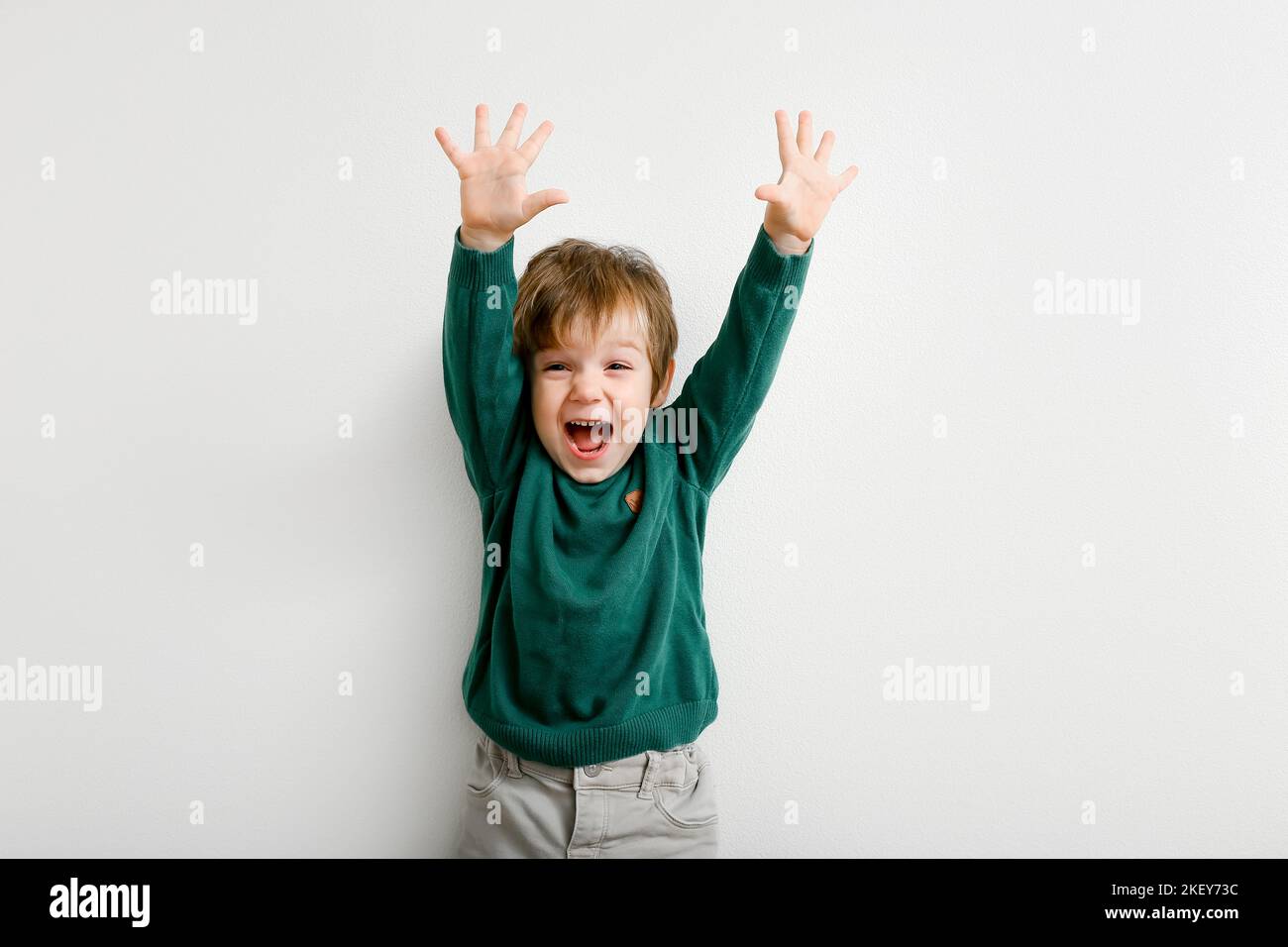 Cute little boy with raised hands up with happiness on white wall ...
