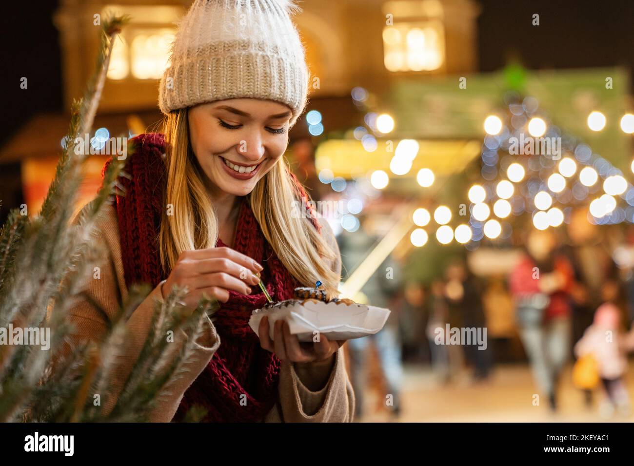 Portrait of happy young woman eating donuts on the christmas market ...