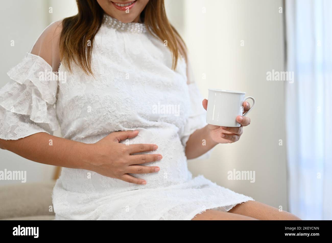 Happy Asian pregnant woman touching her belly with love, feeling her ...