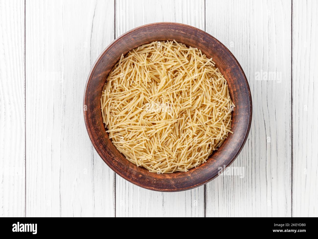 Uncooked vermicelli pasta in ceramic bowl on white wooden background ...