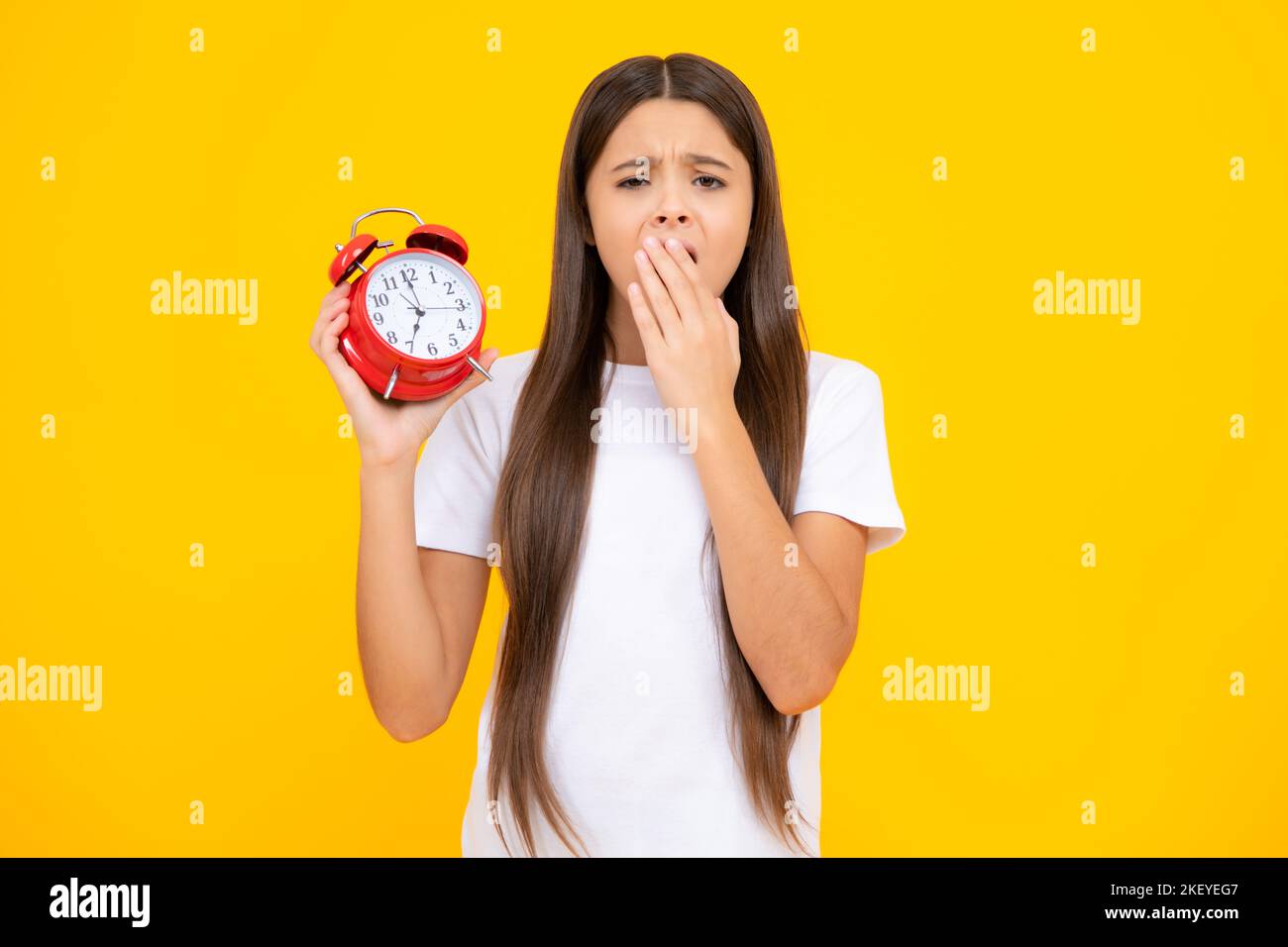 Tired and bored teenager girl. Child holding clock over yellow ...