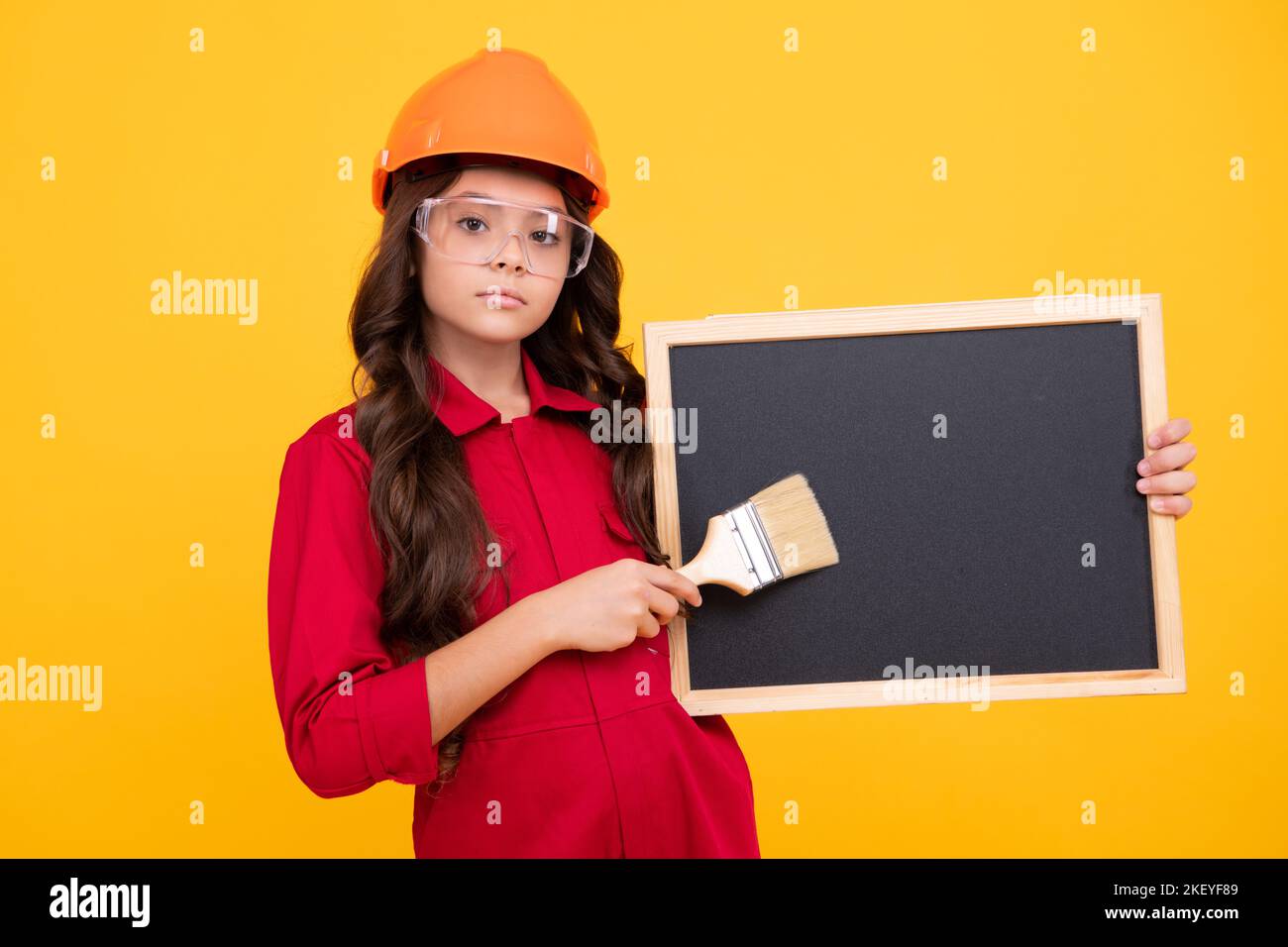 Child builder in helmet. Teenage girl painter with painting brush tool ...