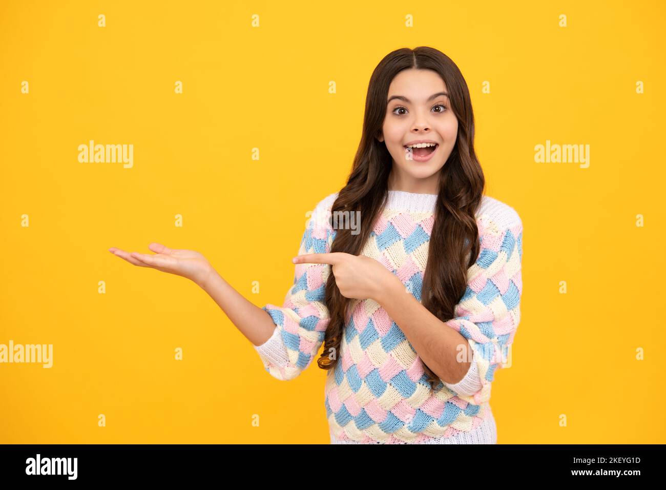 Positive teenager child points aside with cheerful expression, shows ...