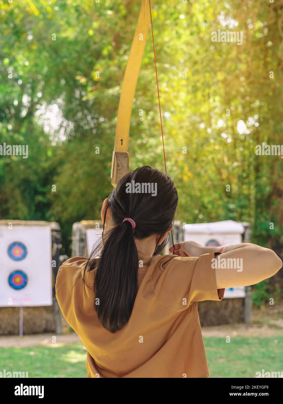 Back view of Asian girl wear face mask aims archery bow and arrow to ...
