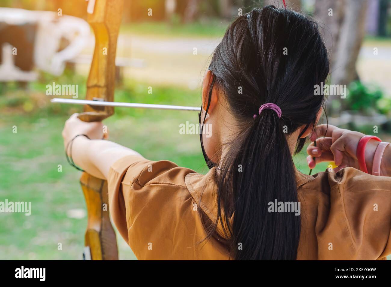 Back view of Asian girl wear face mask aims archery bow and arrow to ...
