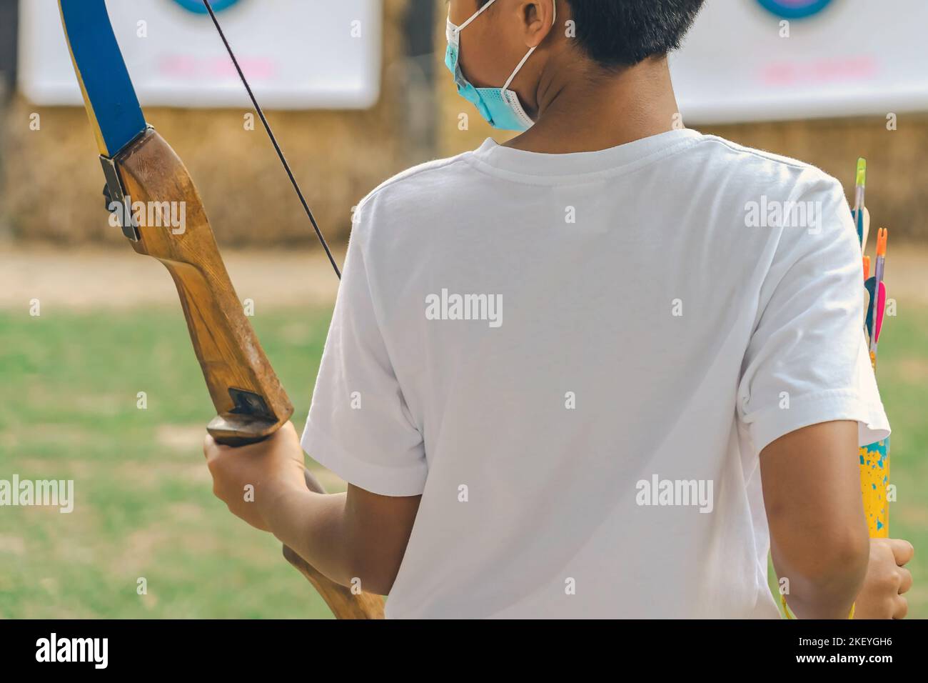 Back view of Asian boy wear face mask aims archery bow and arrow to ...