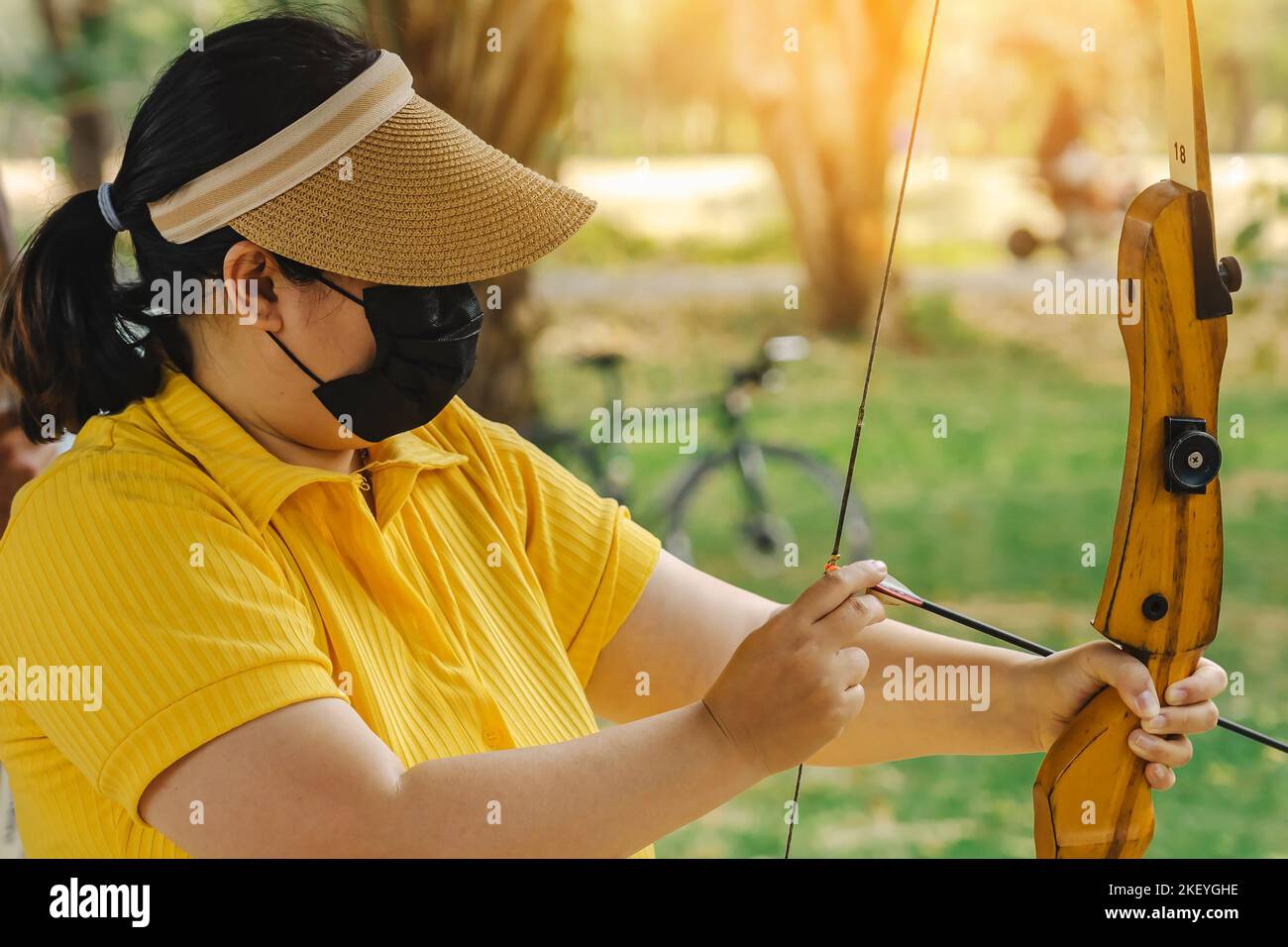 Asian woman wear visor with face mask aims archery bow and arrow to ...