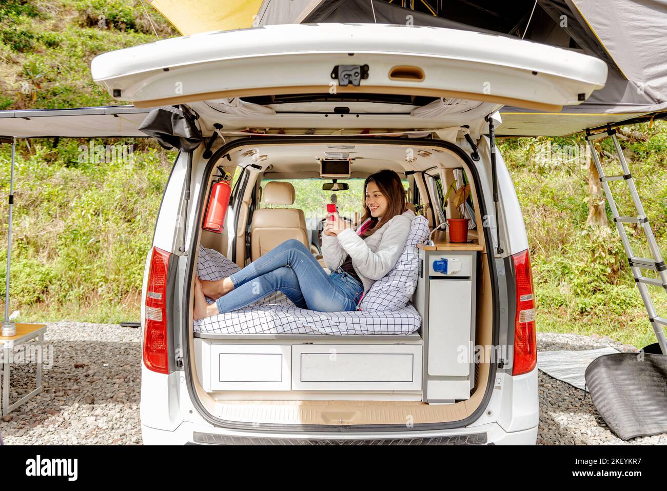 Asian woman using mobile phone inside the campervan enjoying camp ...