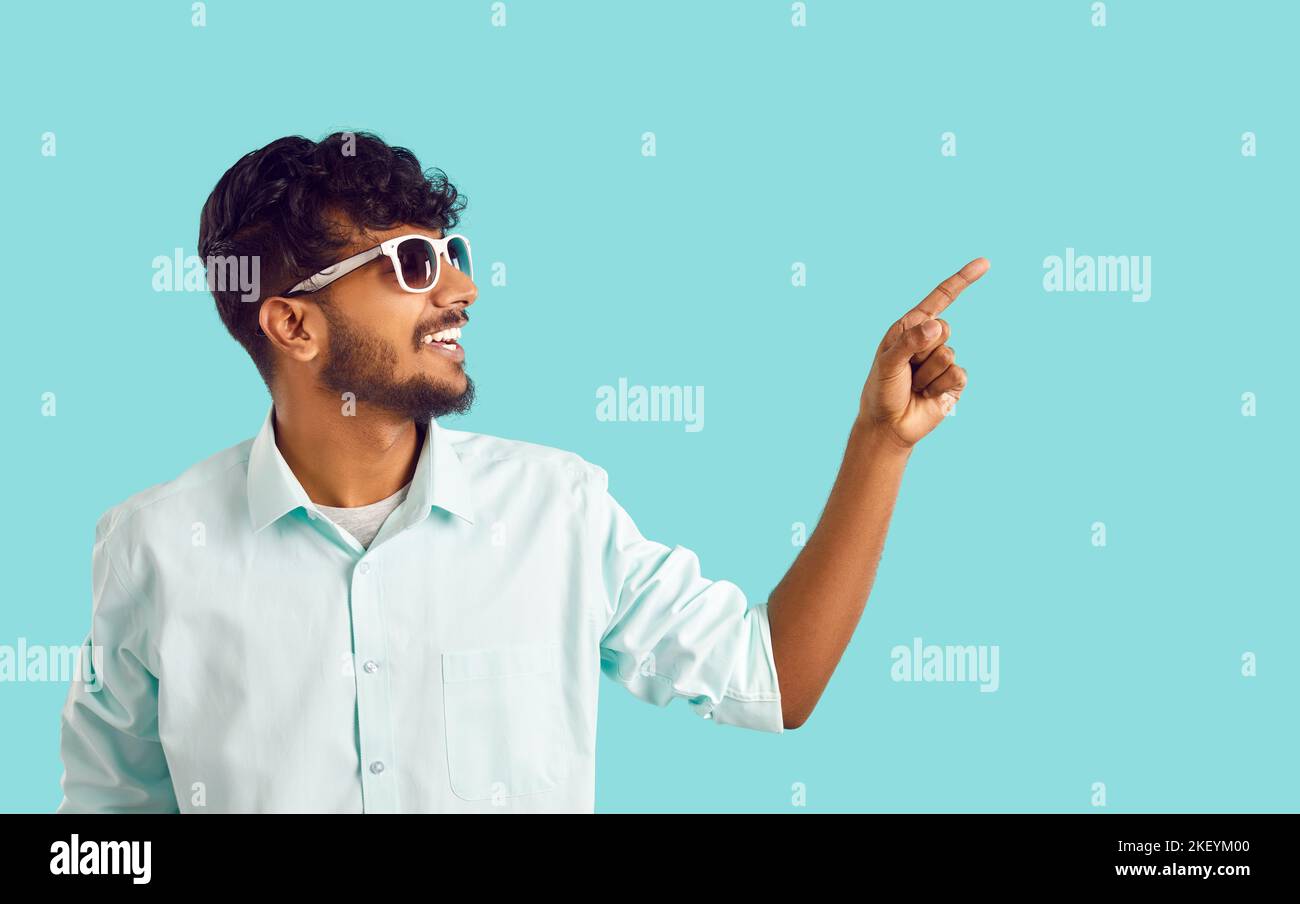 Smiling young man pointing finger looking at copy space on light blue ...