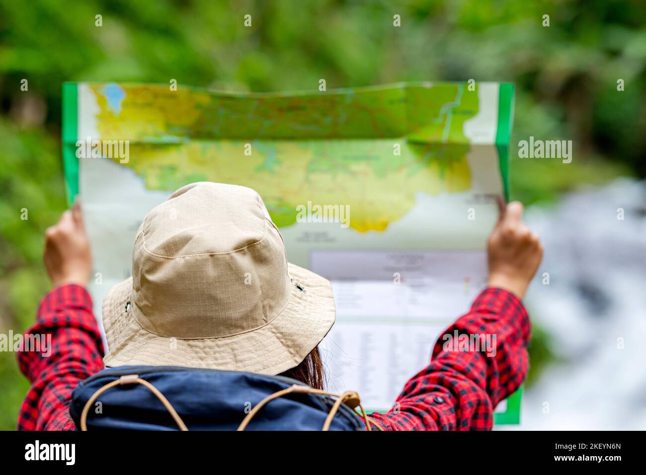 Rear view of Asian woman in a hat and backpack holding maps in the ...
