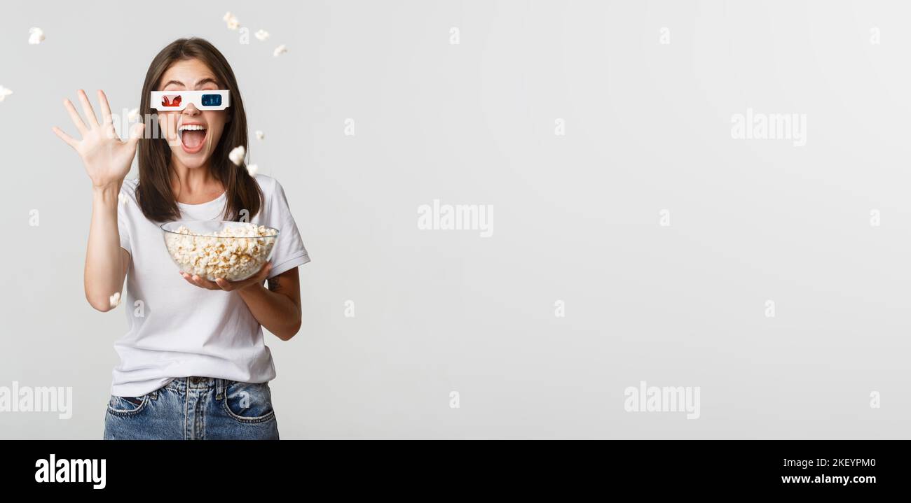 Joyful attractive young girl in 3d glasses, throwing popcorn at screen while watching movie ...