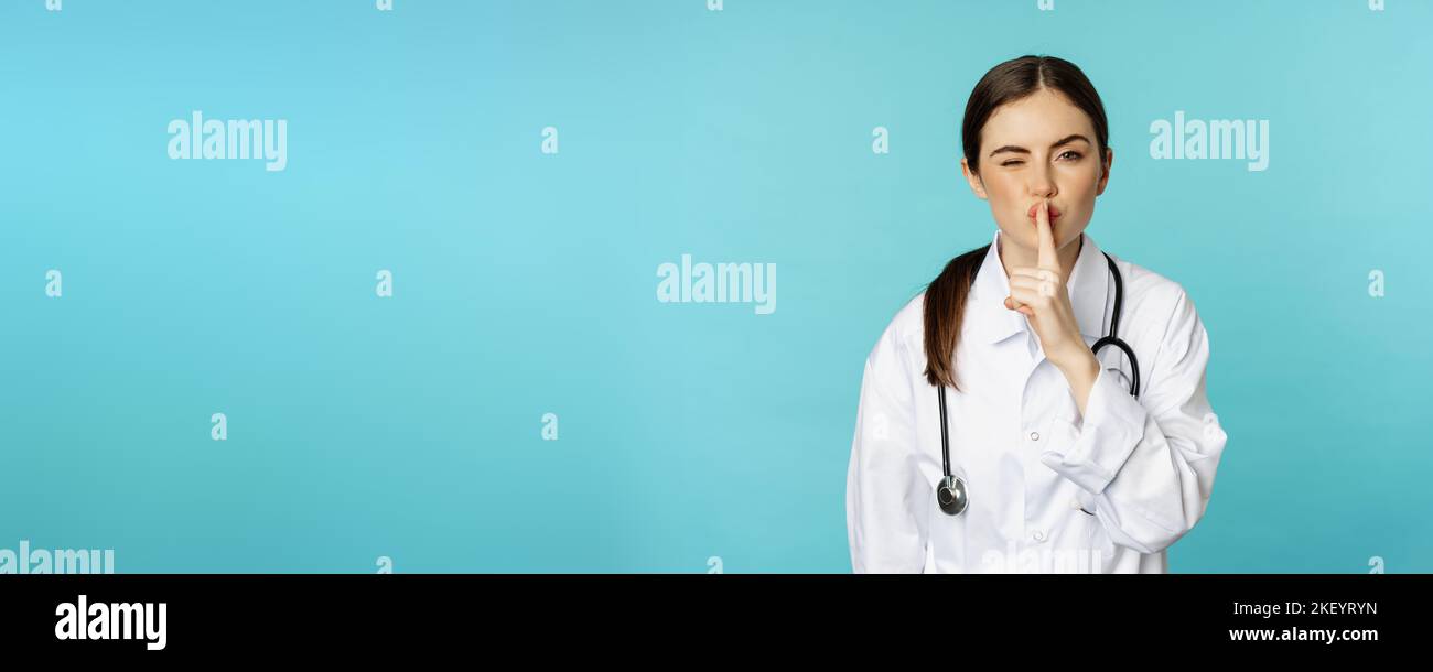 Smiling cute doctor woman, shush, press hush shh sign with finger ...