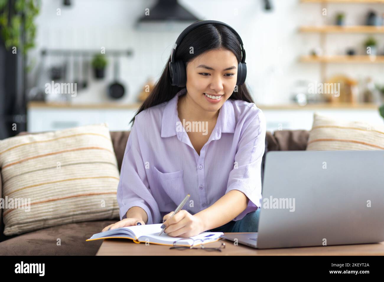 female student studying remotely using a laptop, taking notes on ...