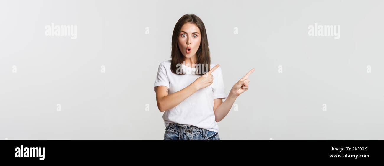 Excited beautiful girl smiling, pointing fingers upper left corner and ...
