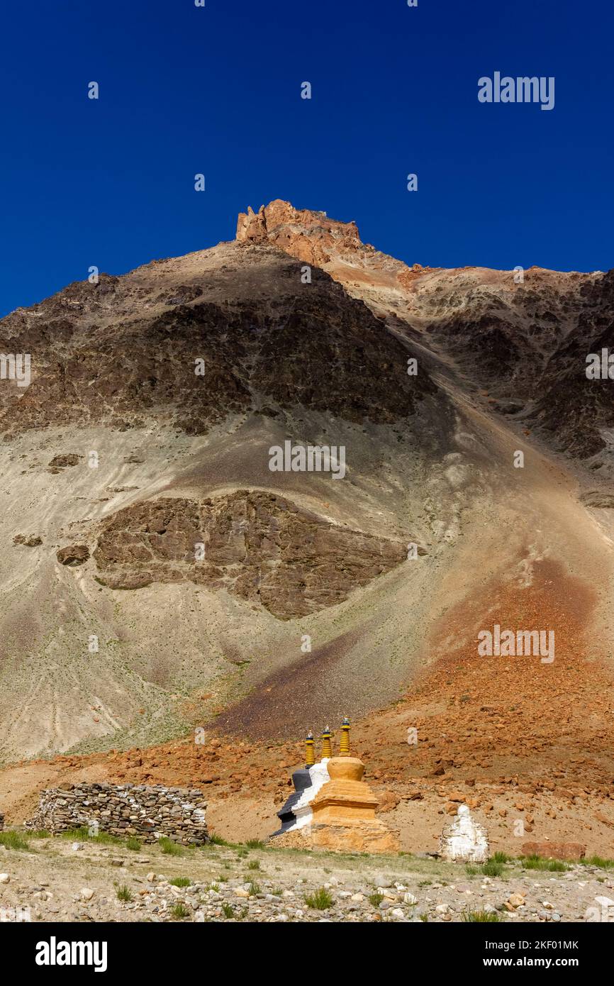 Tibetan Buddhist stupas on the barren slopes below high rocky mountain ...