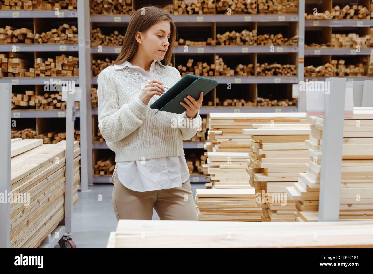 Woman with tablet in a timber and lumber warehouse or hardware store ...