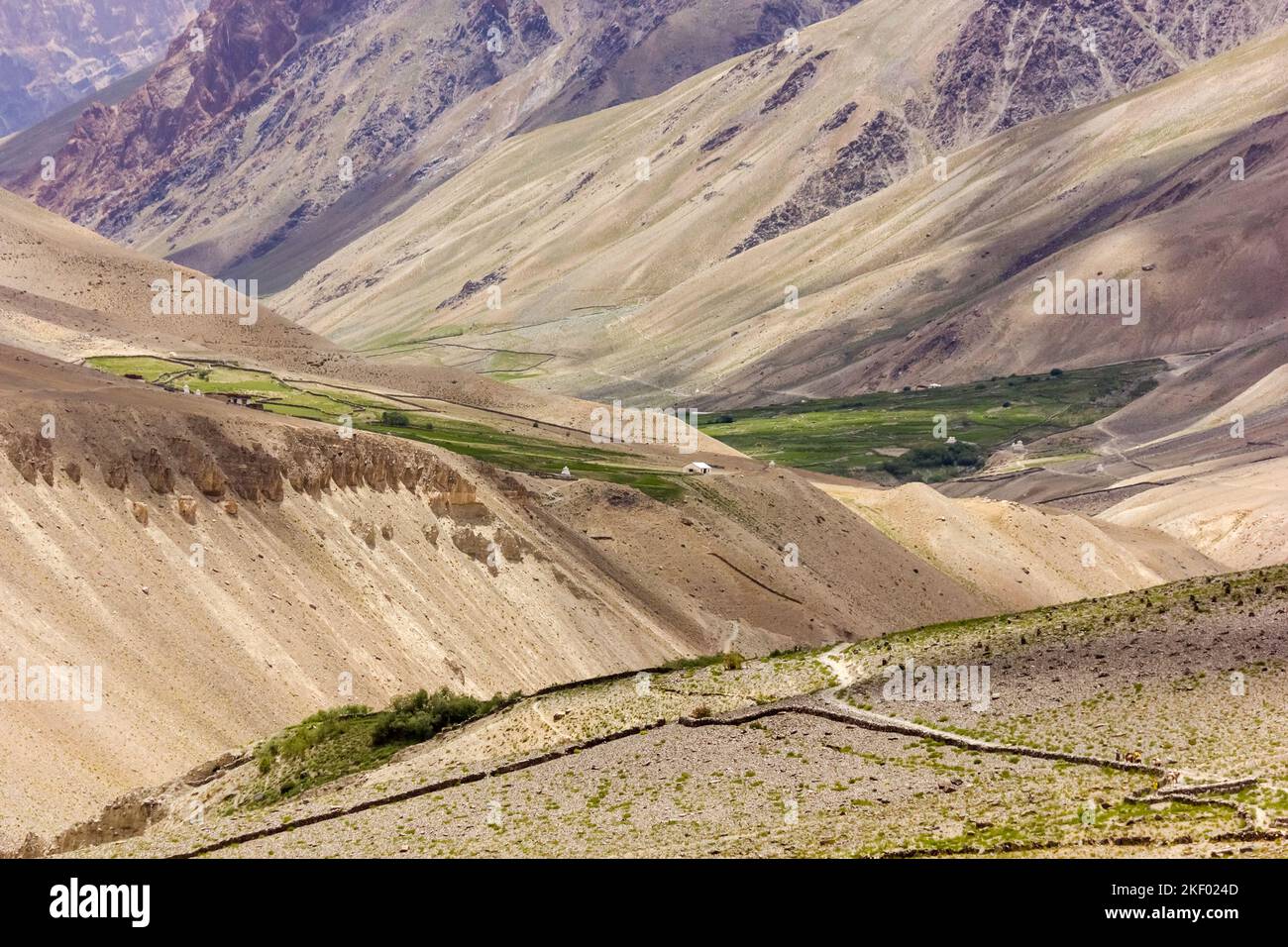 Green fields on the rocky barren brown slopes of the mountains in a ...