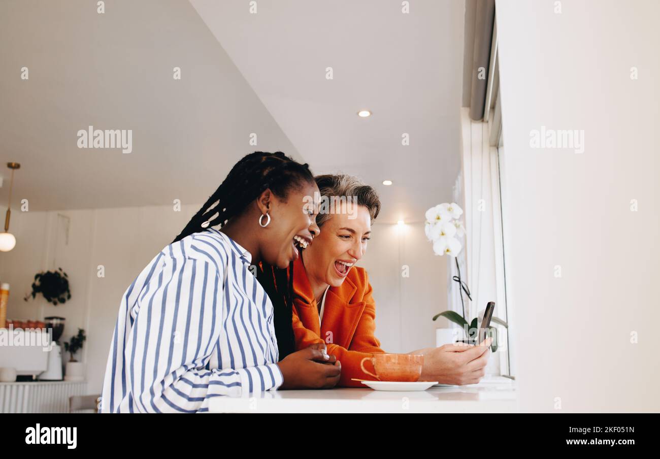 Two happy business women laughing excitedly while using a smartphone ...