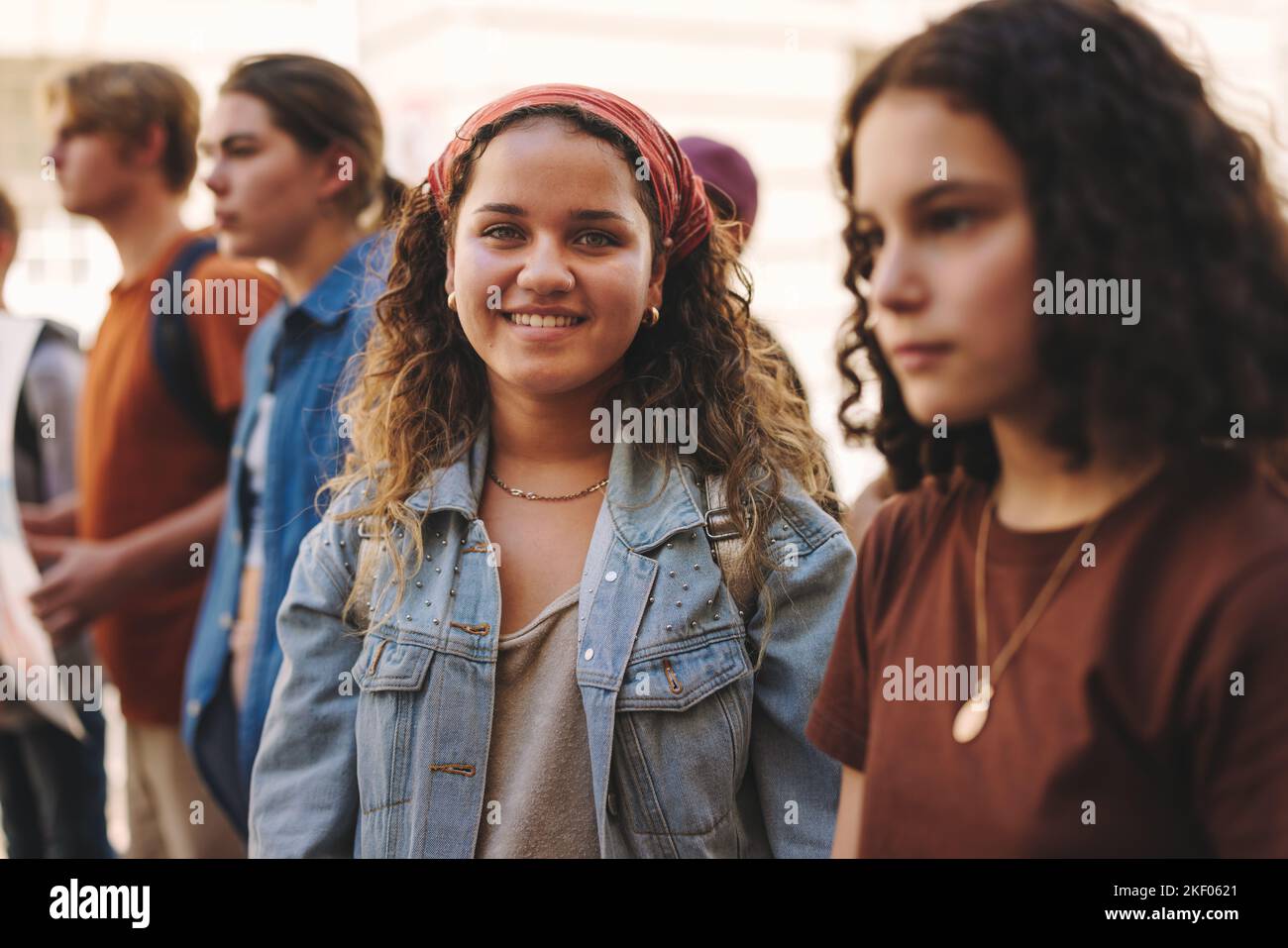 Happy teenage girl smiling at the camera while standing with a group of ...