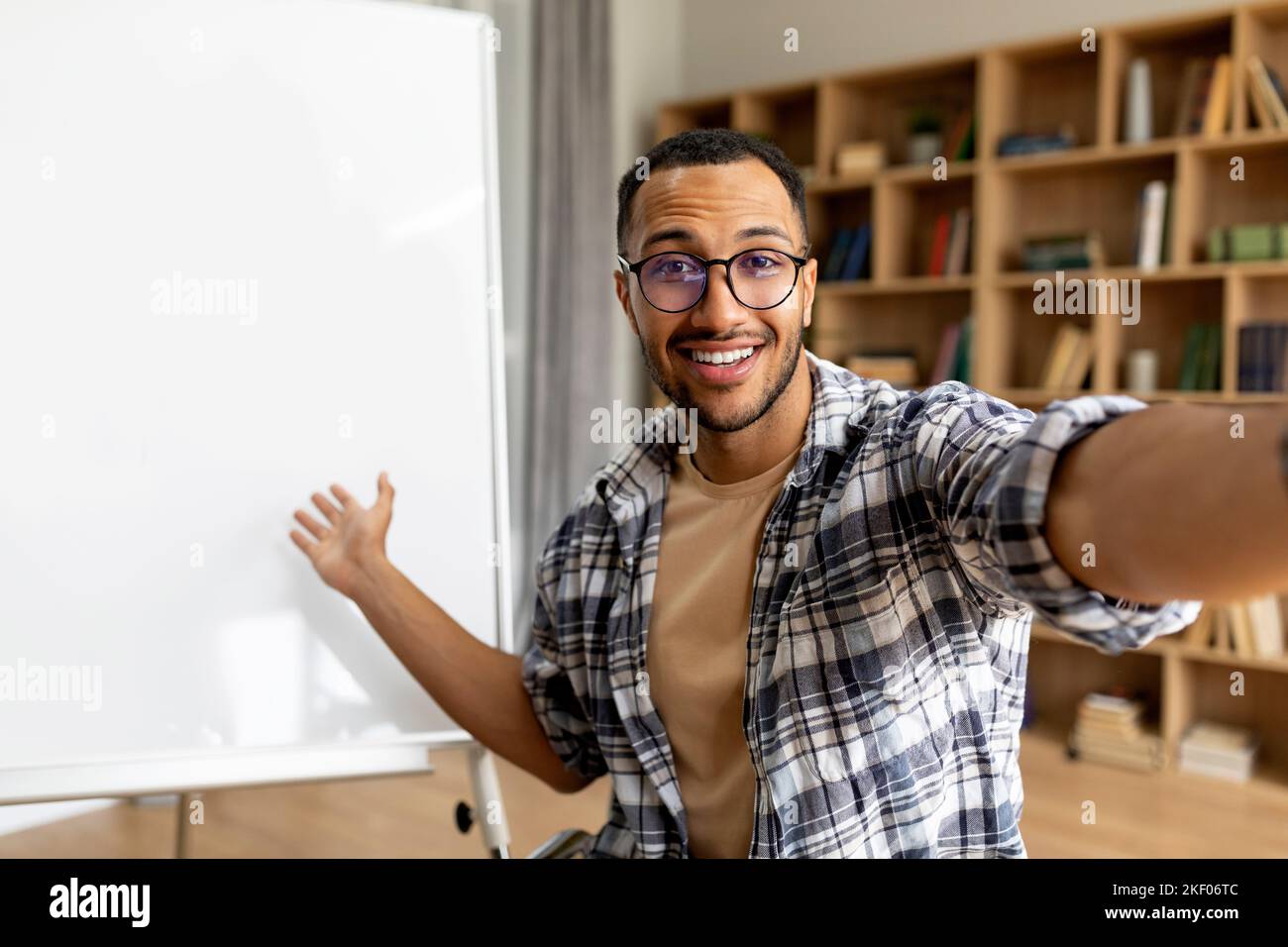 Cheerful arab tutor man smiling to camera and pointing at whiteboard ...