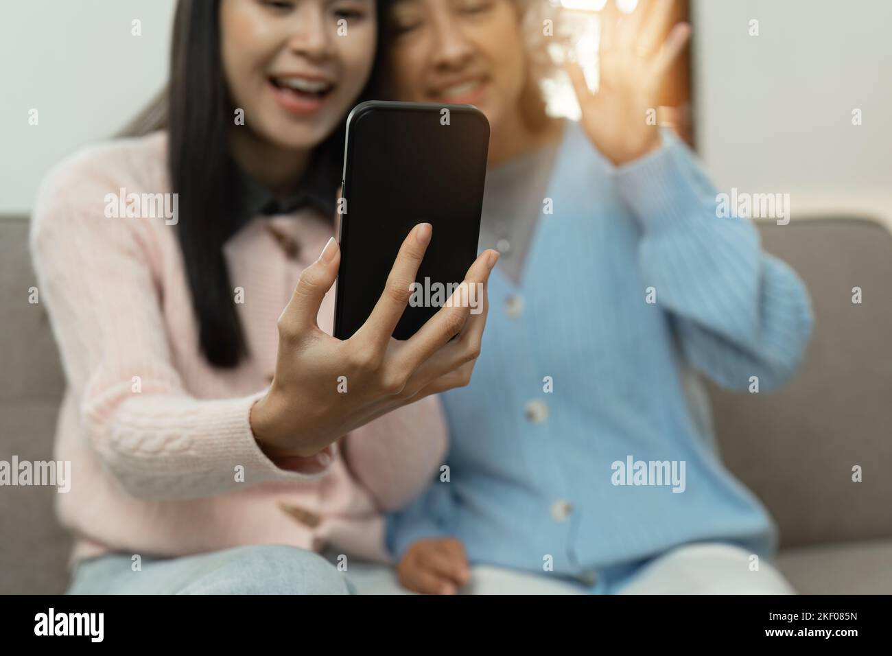 Senior woman and adult daughter look at cell phone screen communicating with family. older woman ...