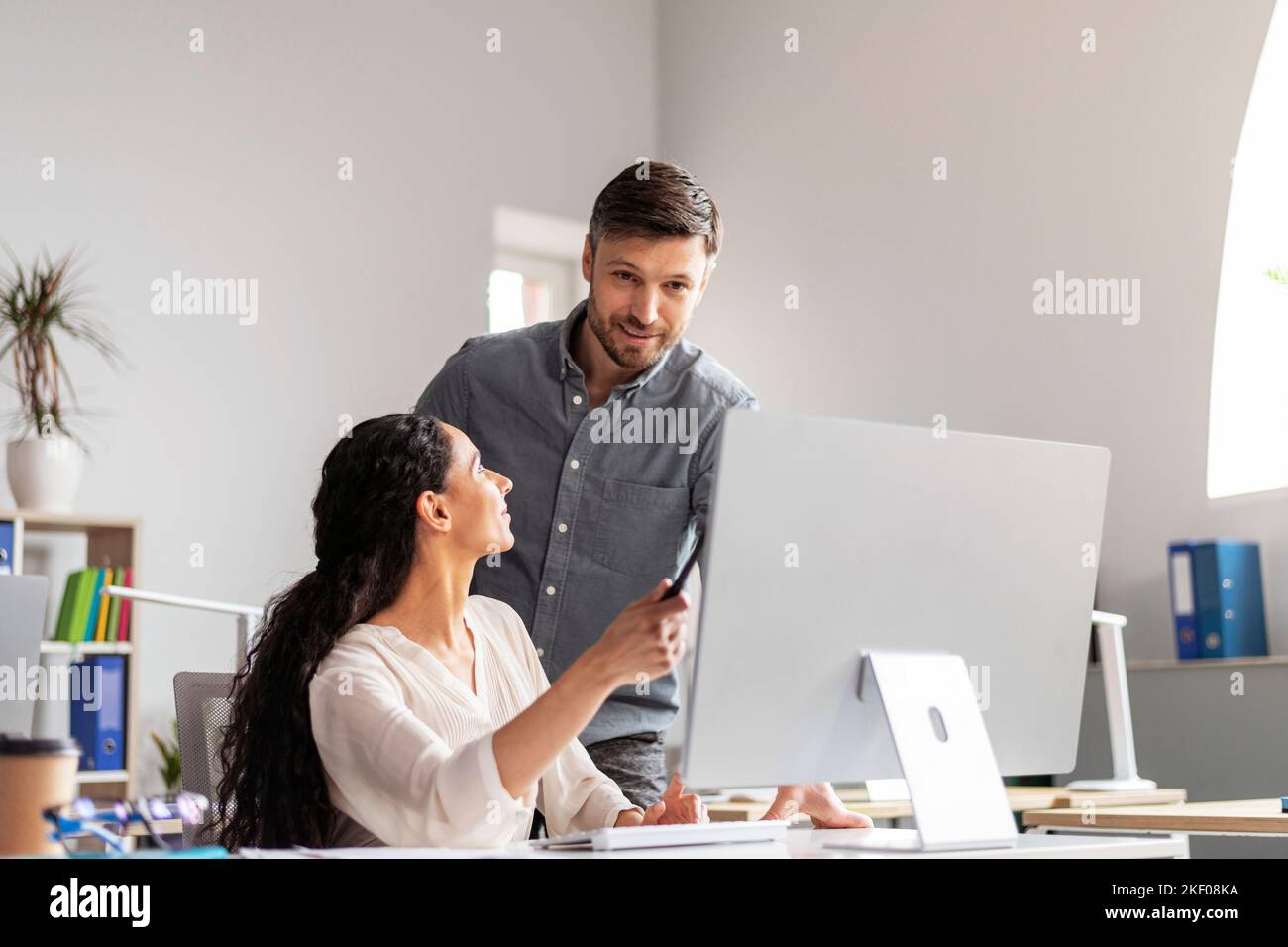 Happy busy millennial european lady showing to man manager with hand to ...