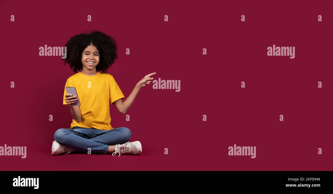 Cheerful black kid chilling on floor with smarpthone, copy space Stock ...