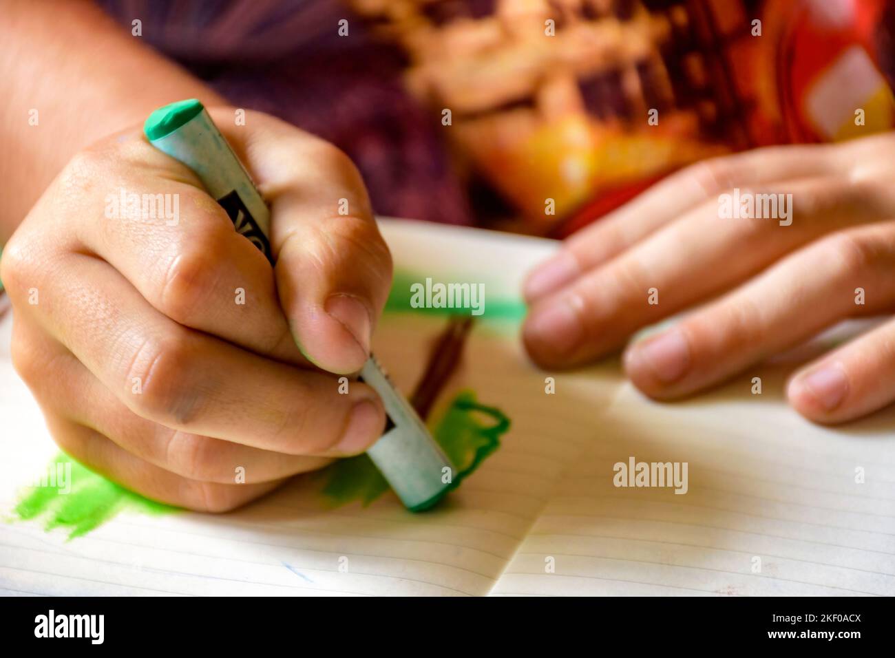 Young child's hands drawing with crayon on a sheet of paper illuminated ...