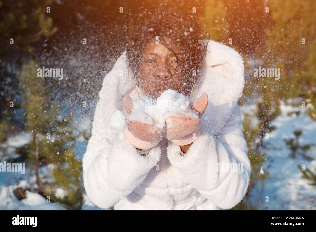 dark-skinned girl blows on snow sparkling under sun rays Stock Photo ...