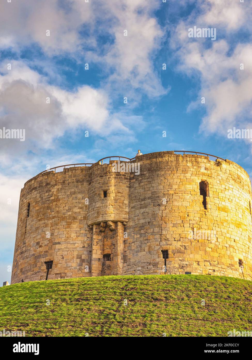 An ancient 13th Century tower is set on a grass embankment. A handrail ...