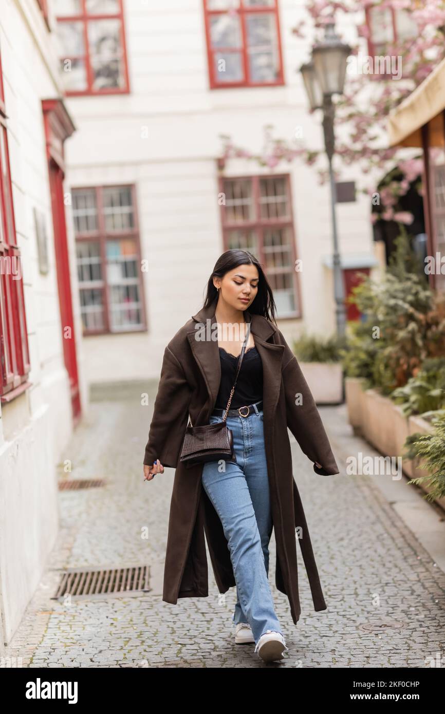 young and pretty woman in trendy autumn clothes walking along narrow ...