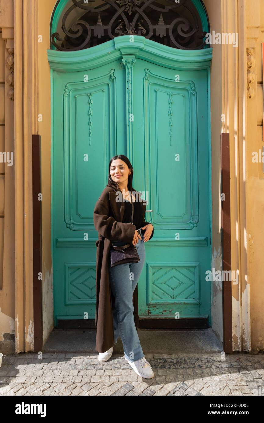 Smiling woman in coat looking at camera near turquoise door of building ...