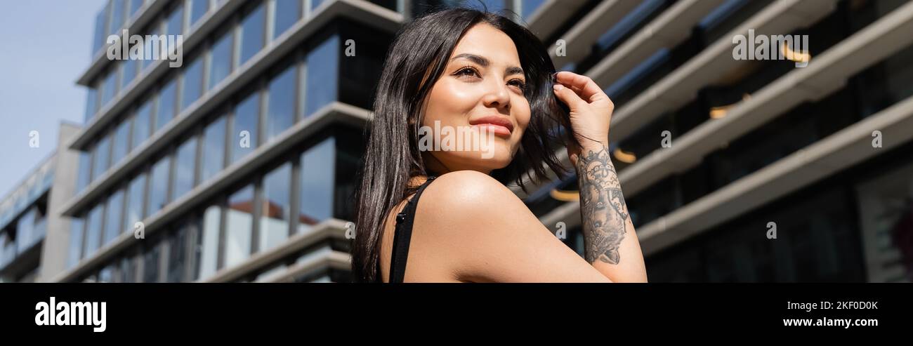 Low angle view of positive tattooed woman looking away on urban street ...