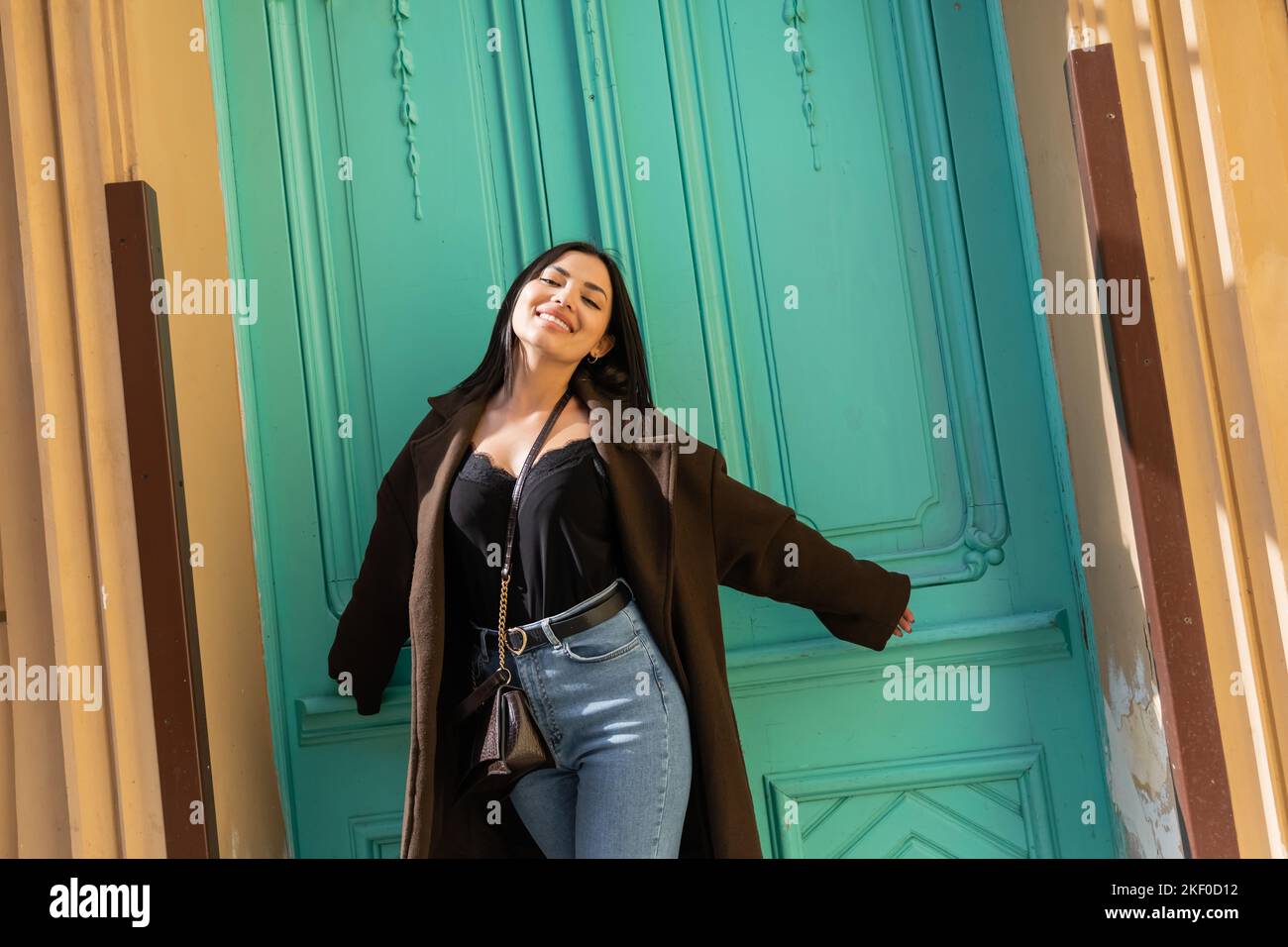 Cheerful traveler looking at camera near turquoise door of building on ...