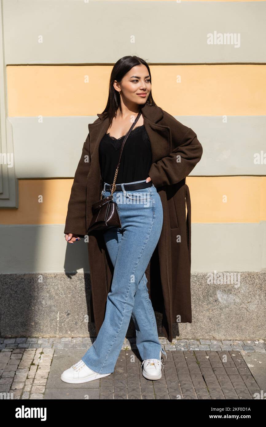 Trendy woman in coat holding hand on hip on urban street,stock image ...