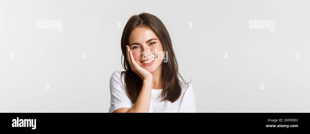 Close-up of beautiful smiling brunette girl touching cheeks, blushing ...