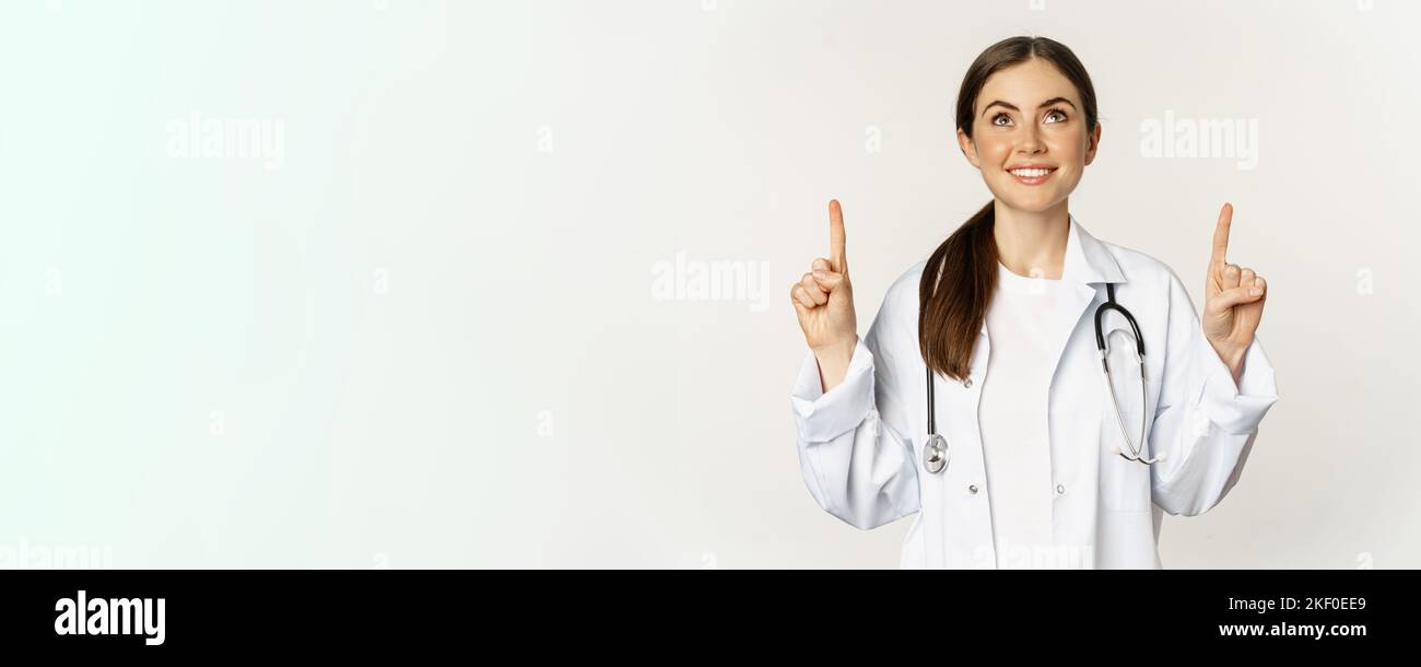 Happy beautiful doctor, female physician pointing fingers up, showing ...