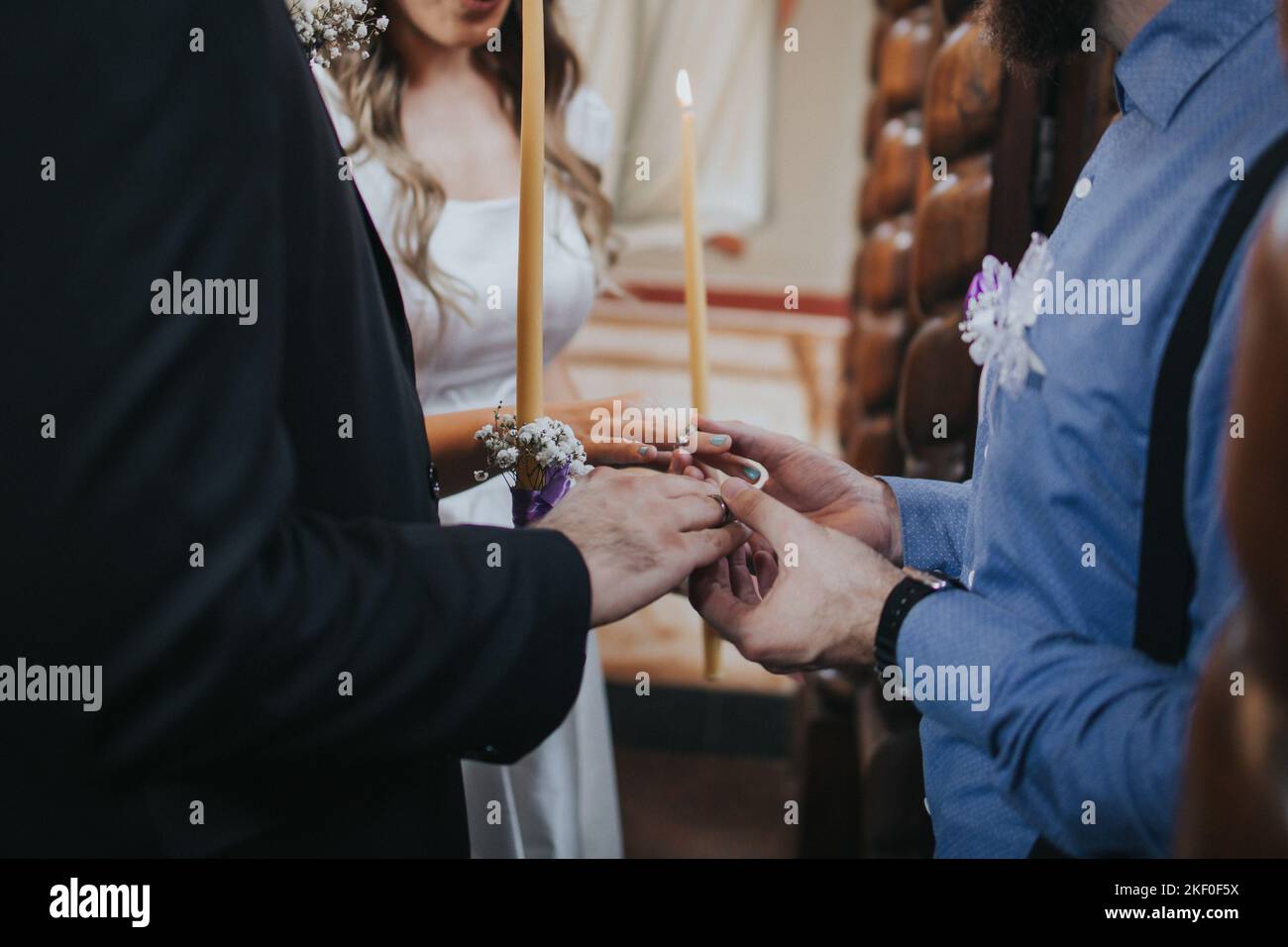 A closeup of groom and bride with wedding rings holding candle with ...