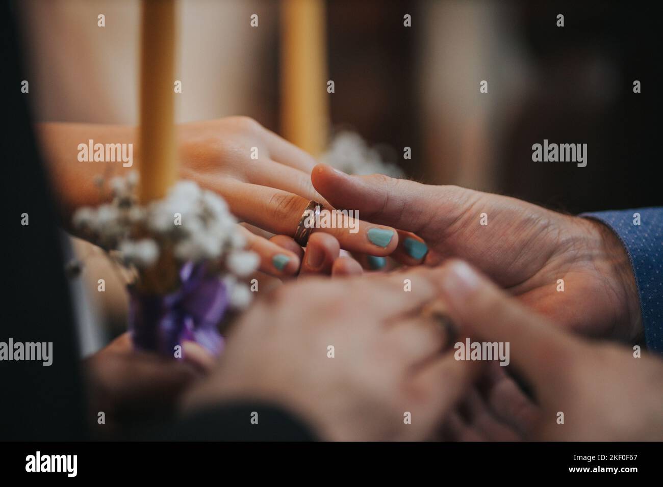 A closeup of groom and bride with wedding rings holding candle with ...