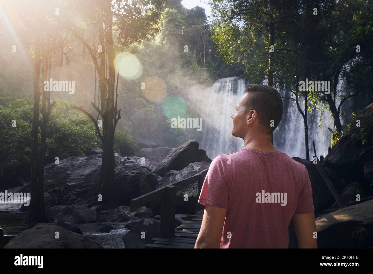 Man walking through rainforest to high waterfall in mountains. Tourist ...