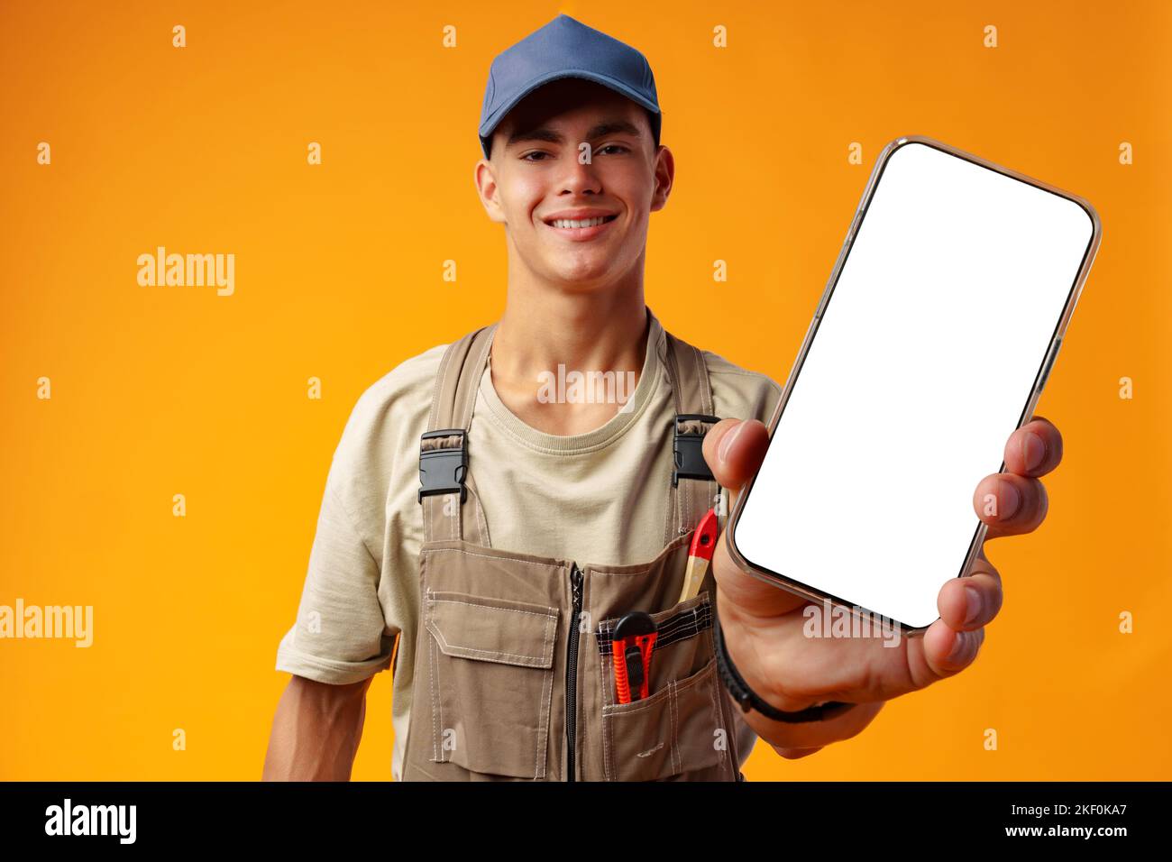 Portrait of handyman in uniform showing blank mobile phone on yellow ...