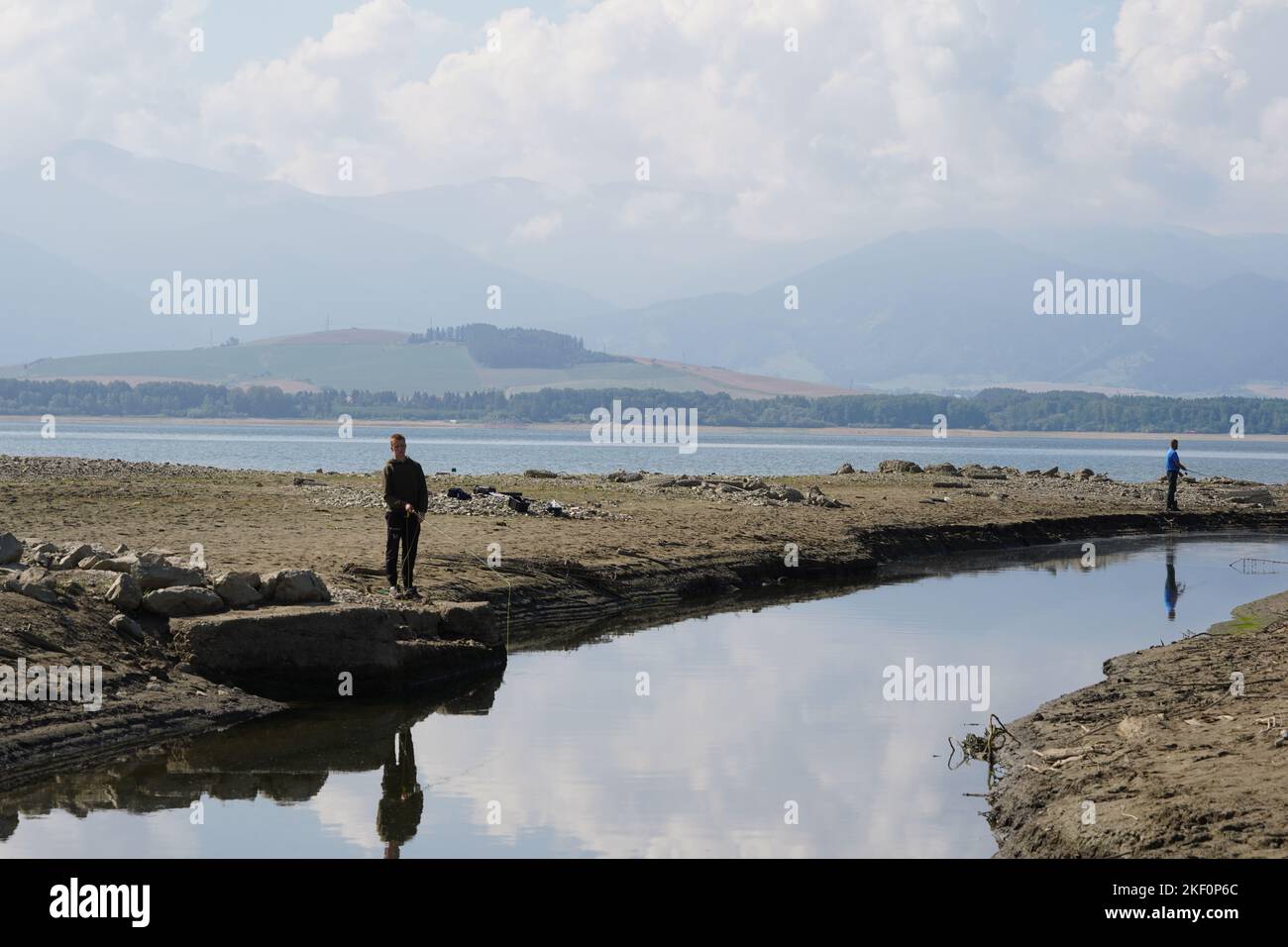 Two anglers fishing in arid or dried up small river channel supplaying ...