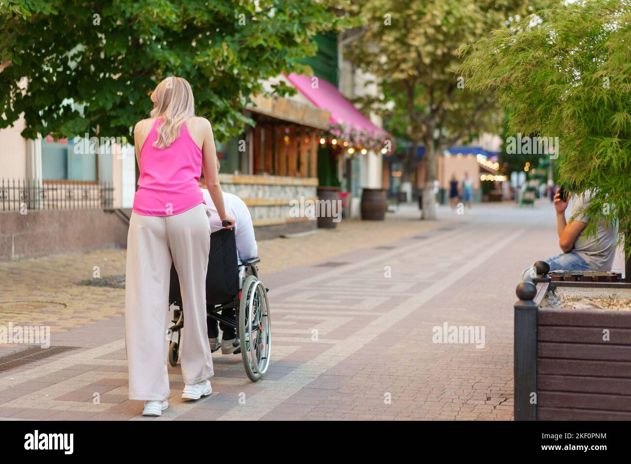 Back view of young woman helping mature woman in wheelchair in the city ...