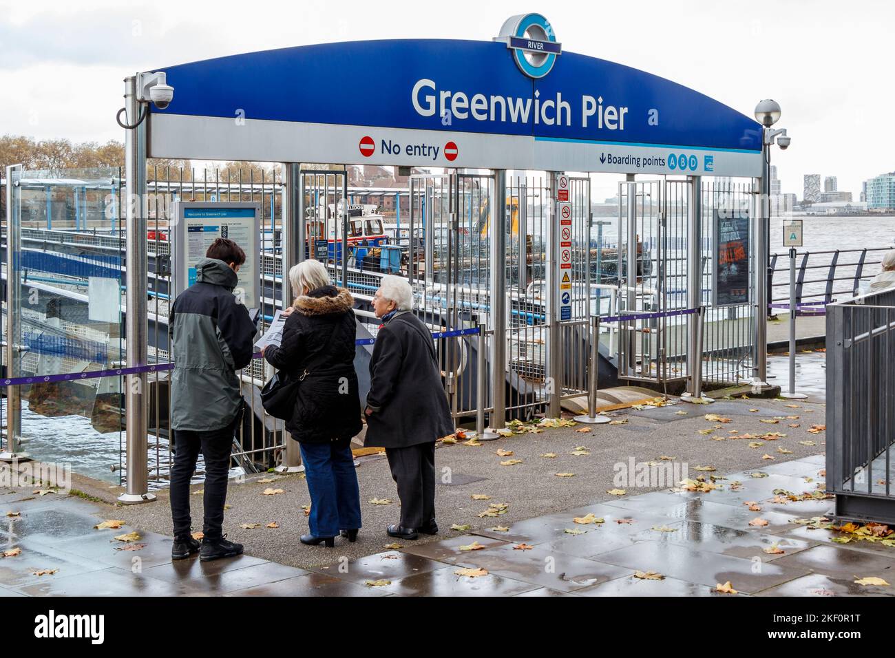 Tourists consult a timetable while waiting for a Thames Clipper at Greenwich Pier, London, UK ...