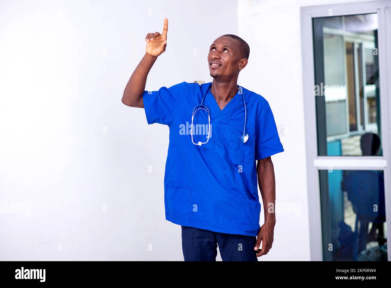 young male doctor in blue uniform with stethoscope pointing finger up ...