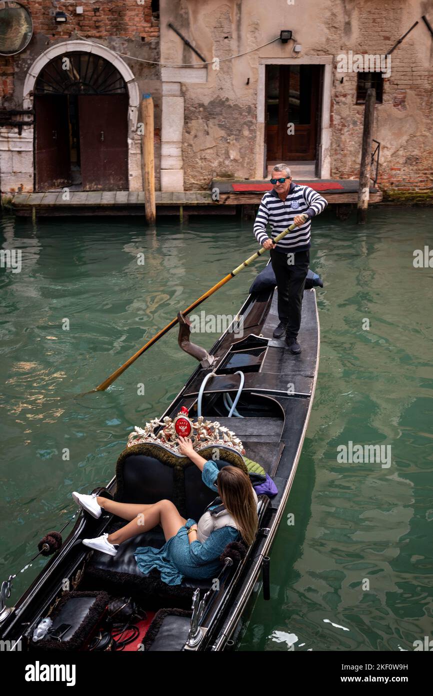 Gondolier steering the gondola with a young female passenger on a canal ...